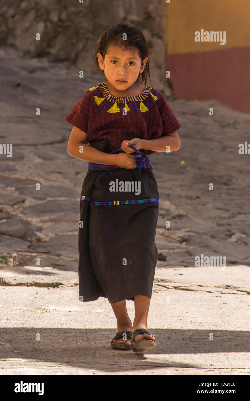 A young Mayan girl wearing traditional dress walks down the cobblestone ...