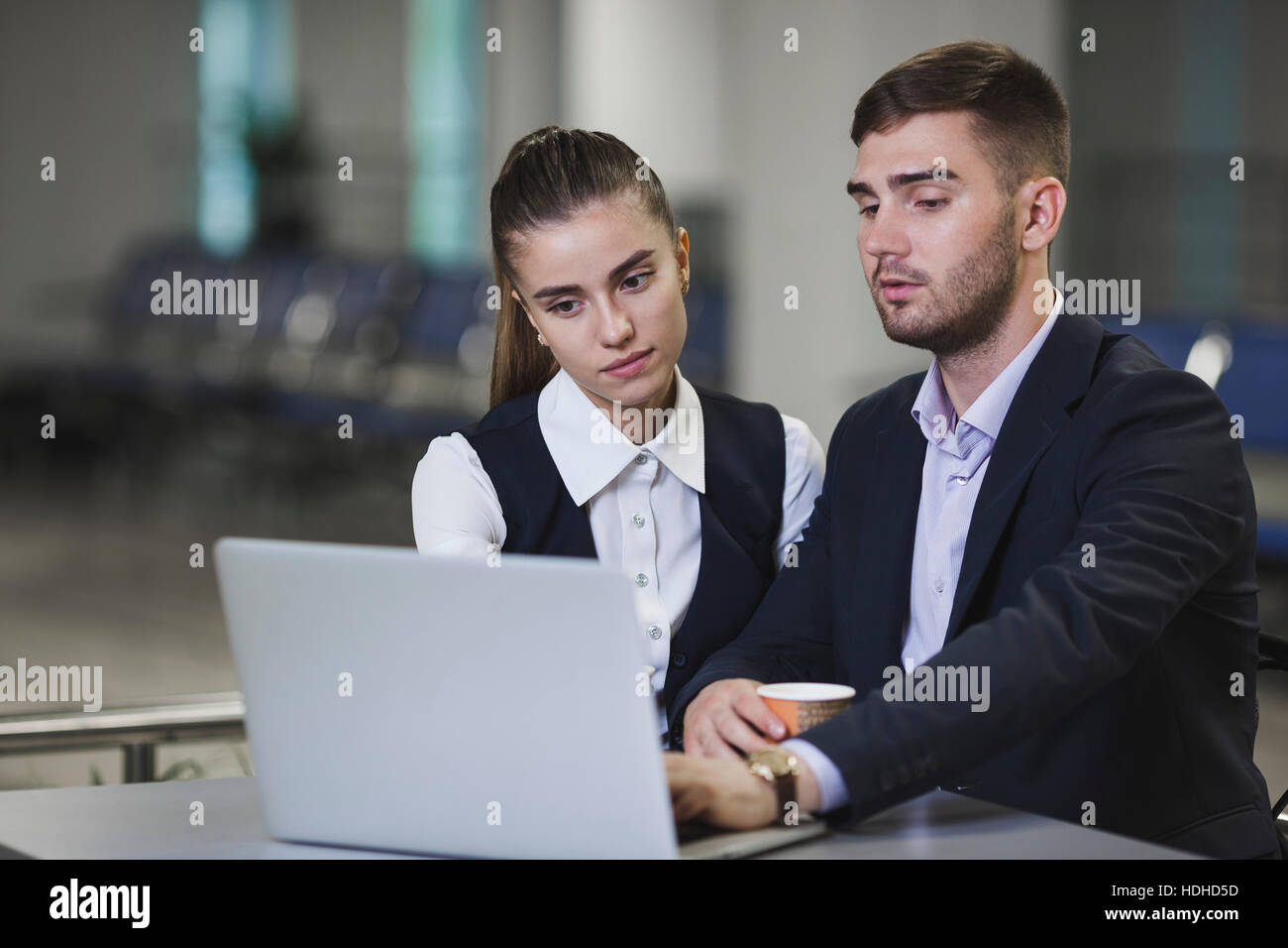 Young businessman and businesswoman using laptop at table in airport ...