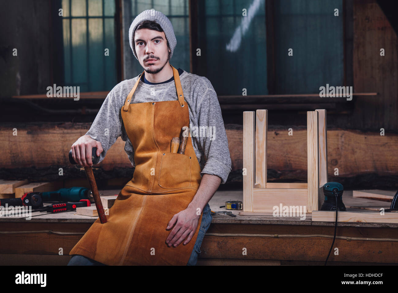 Portrait of carpenter holding hammer while sitting on bench at workshop ...