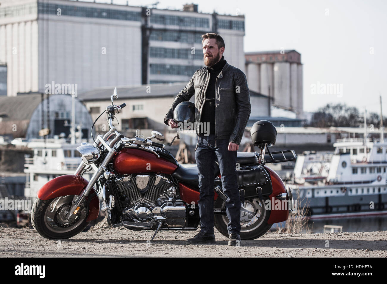 Full length portrait of biker holding helmet while standing by ...