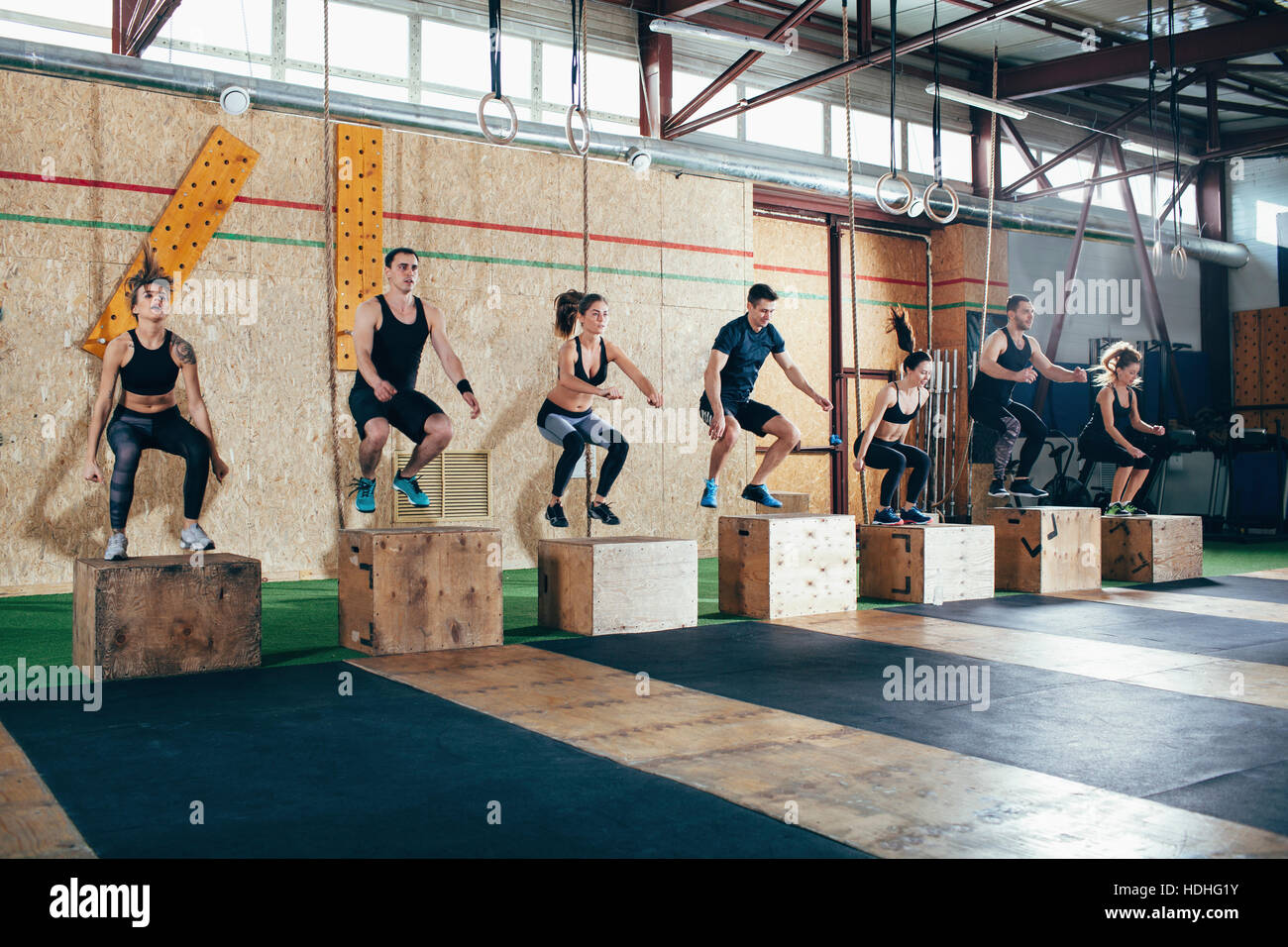 Full length of determined athletes doing box jumping at gym Stock Photo ...