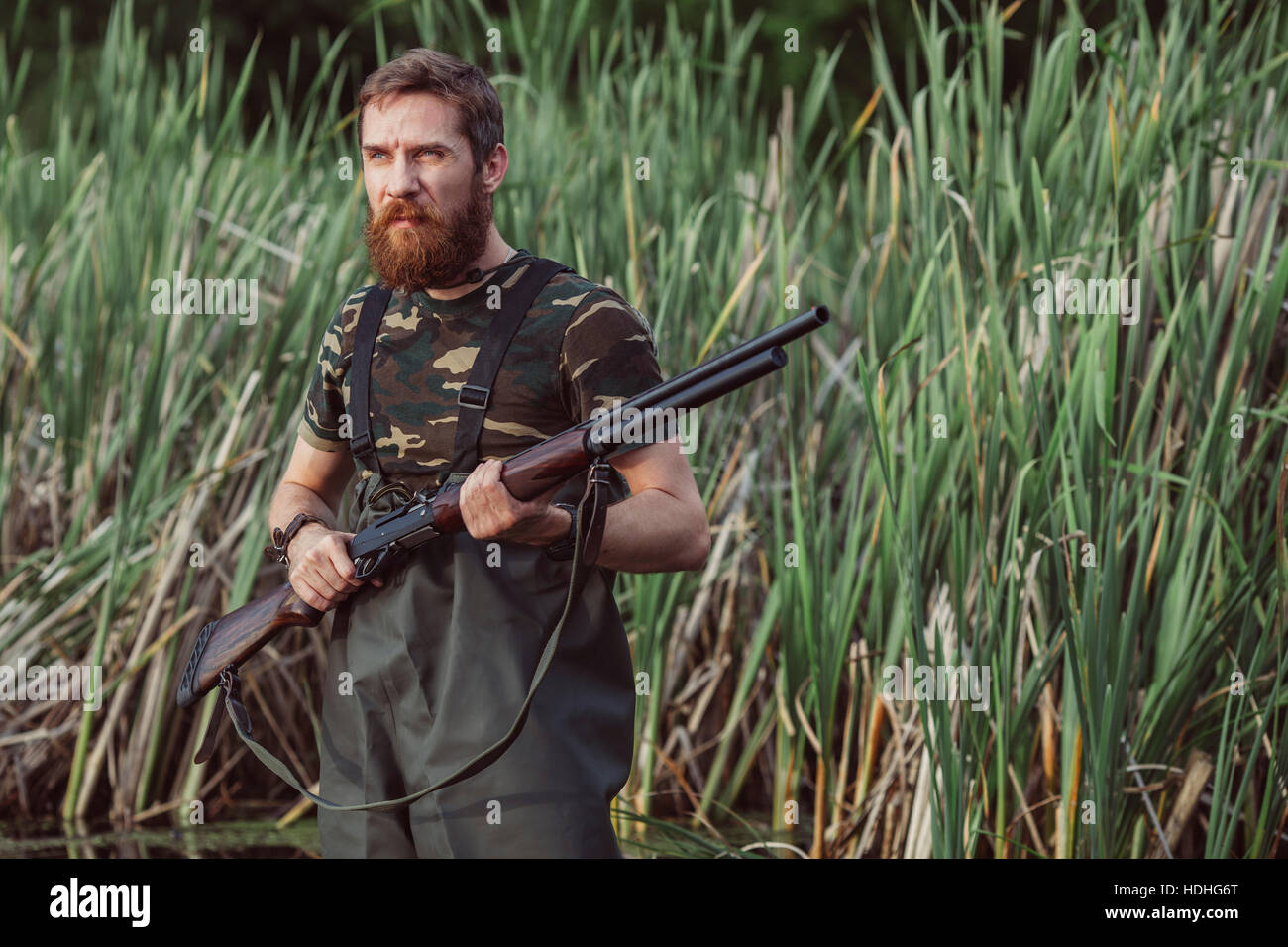 Hunter holding rifle while looking away on grassy field Stock Photo - Alamy