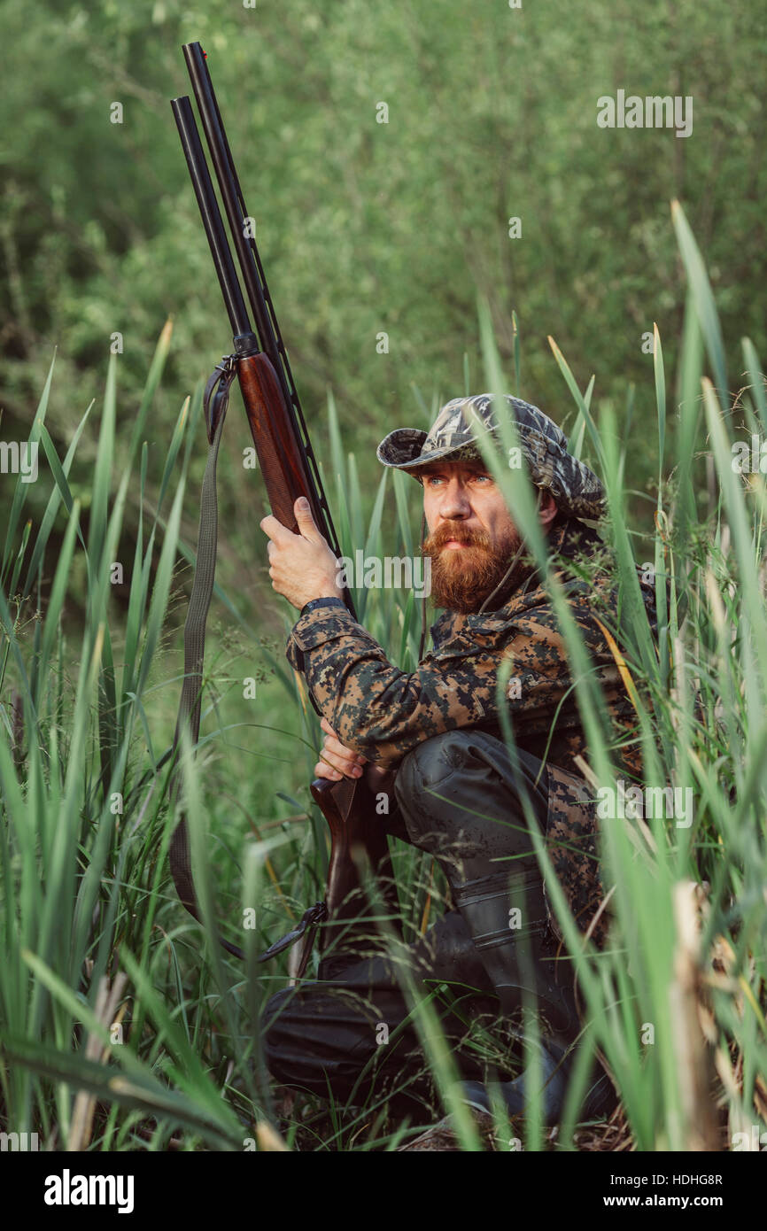 Hunter holding rifle while sitting on field Stock Photo - Alamy