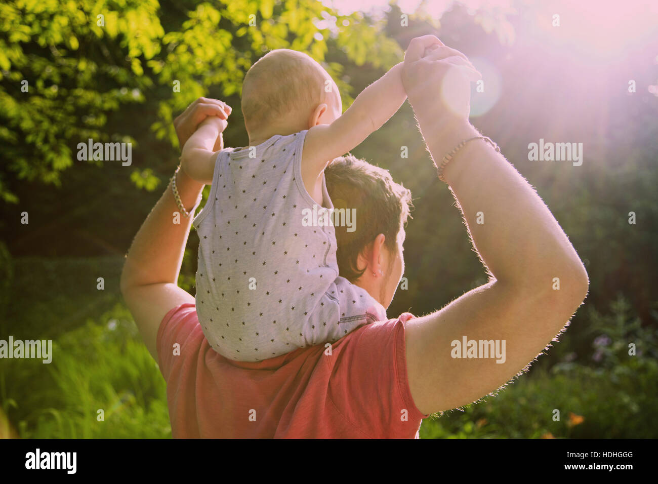 Rear view of father carrying baby boy on shoulders at yard during ...