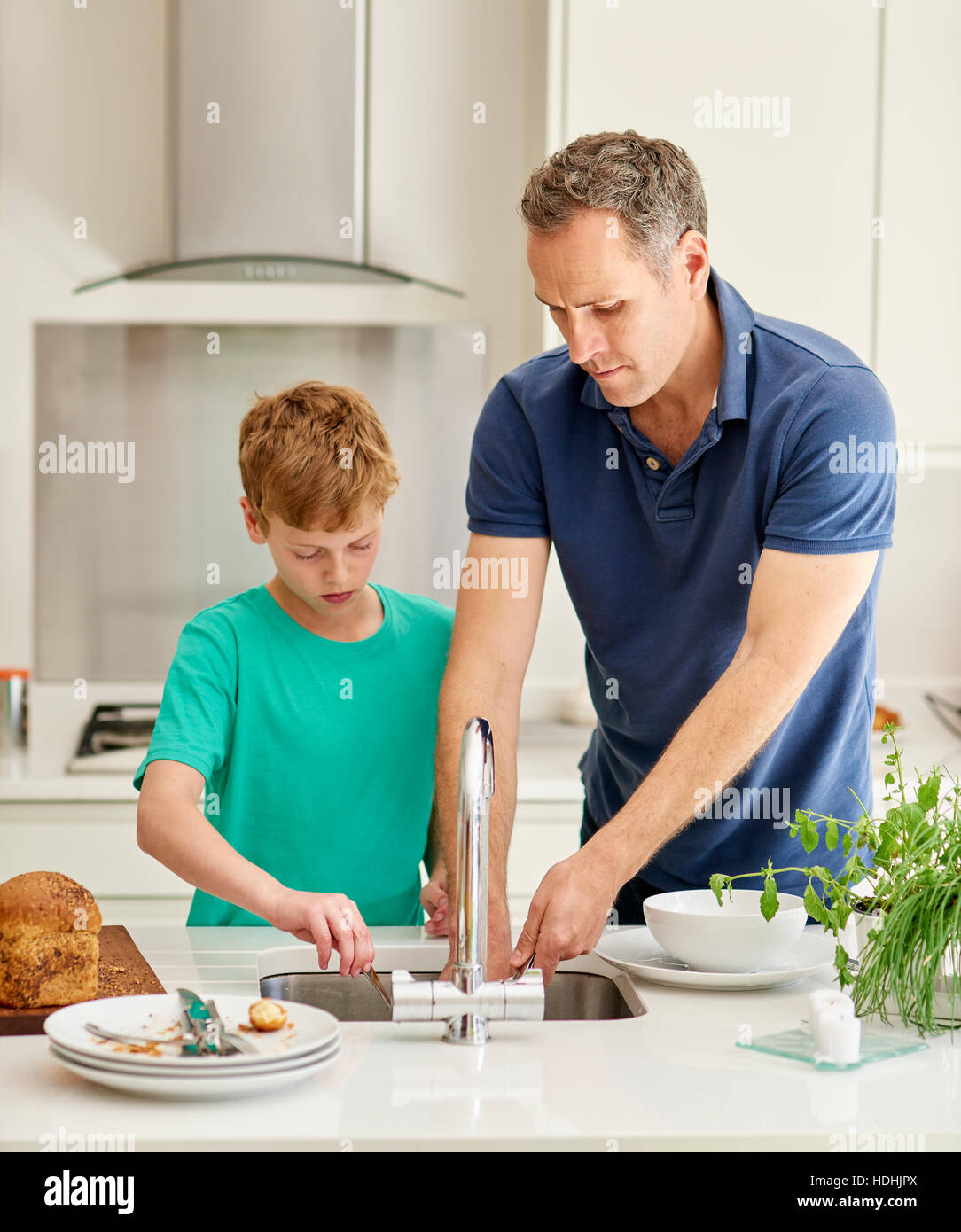 A family home. A man and a young boy in the kitchen side by side doing ...
