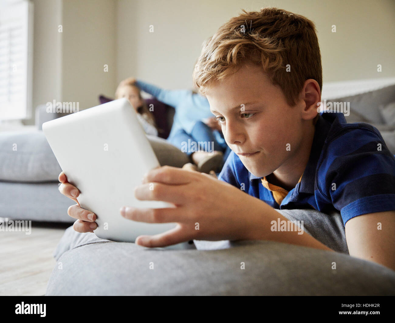 A family home. A boy watching a digital tablet, lying on the floor ...