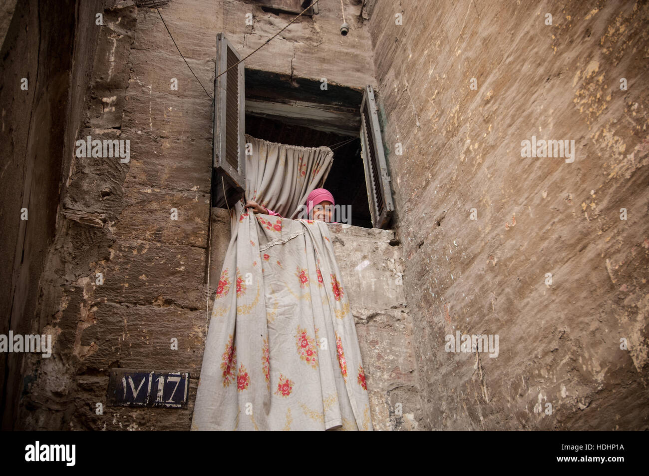 Young Egyptian girl looking from a window in a poor district of Islamic ...