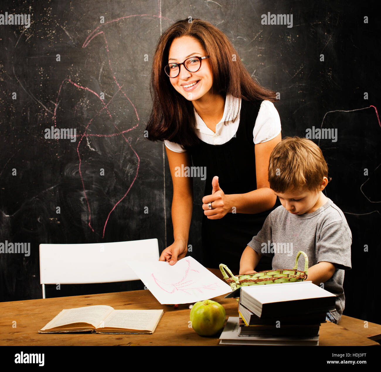 little cute boy with young teacher in classroom studying at blackboard ...