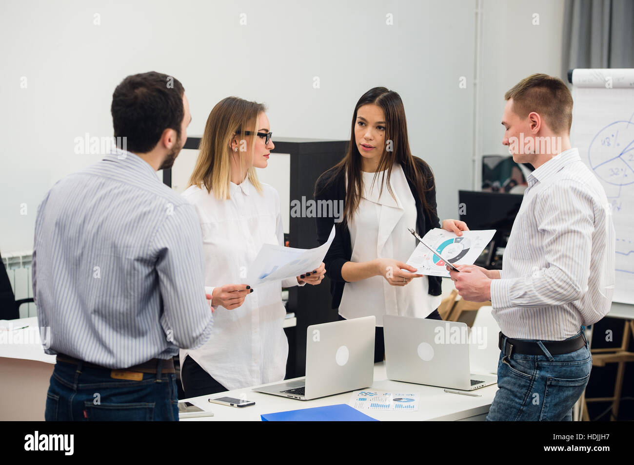 Four young business people working as a team gathered around laptop ...