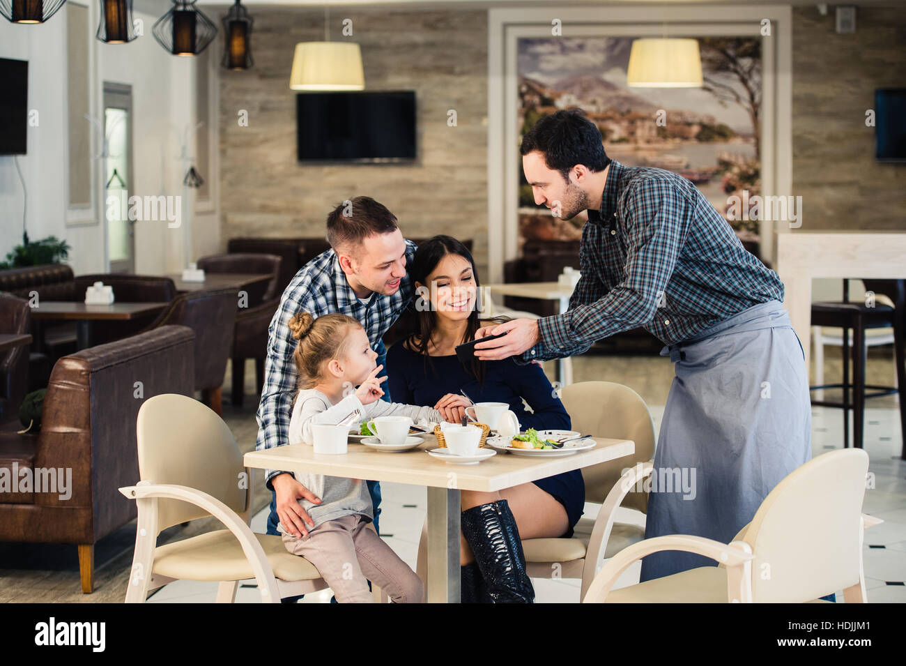 Friendly smiling waiter taking order at table of family having dinner ...
