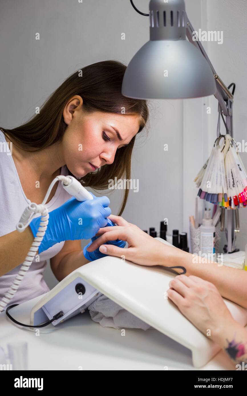 Hardware manicure in a salon. Manicurist is applying electric nail file ...
