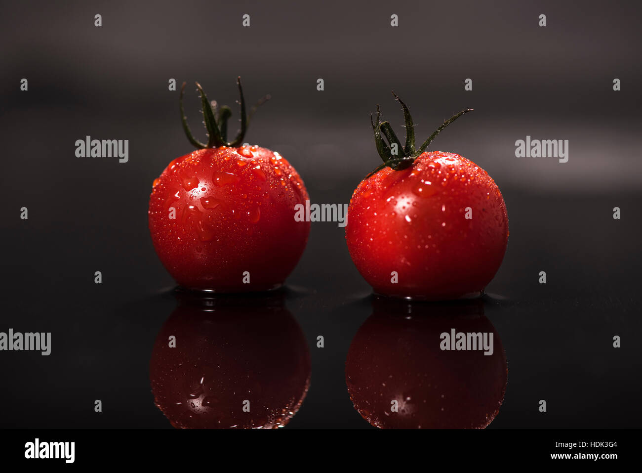 Two ripe, red tomatoes with drops of water on the table, bouncing off ...