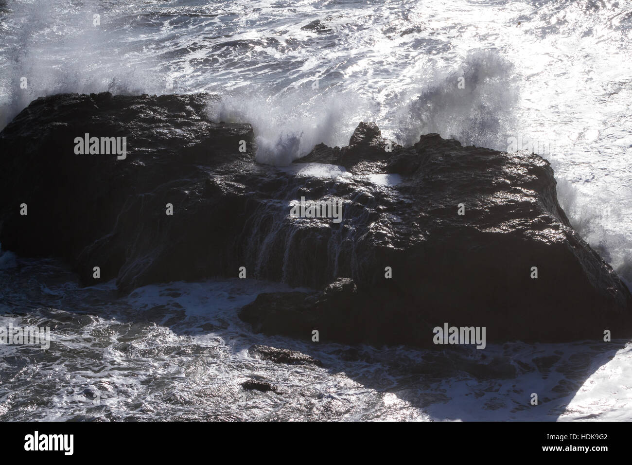 high contrast image with a dark large rock and powerful waves crashing ...