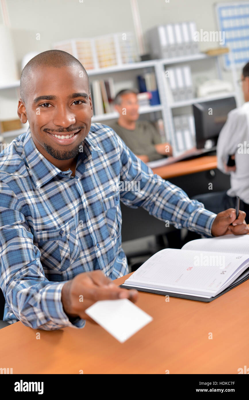 Man sat at desk passing a business card Stock Photo - Alamy