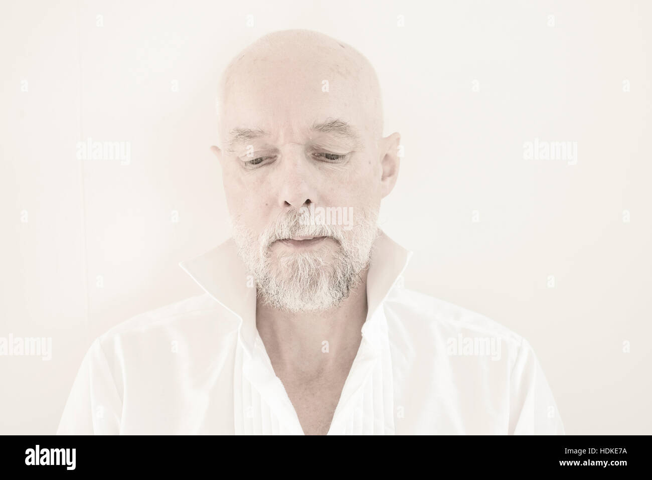 Sad and pensive old man looking down. He is wearing a white unbuttoned ...