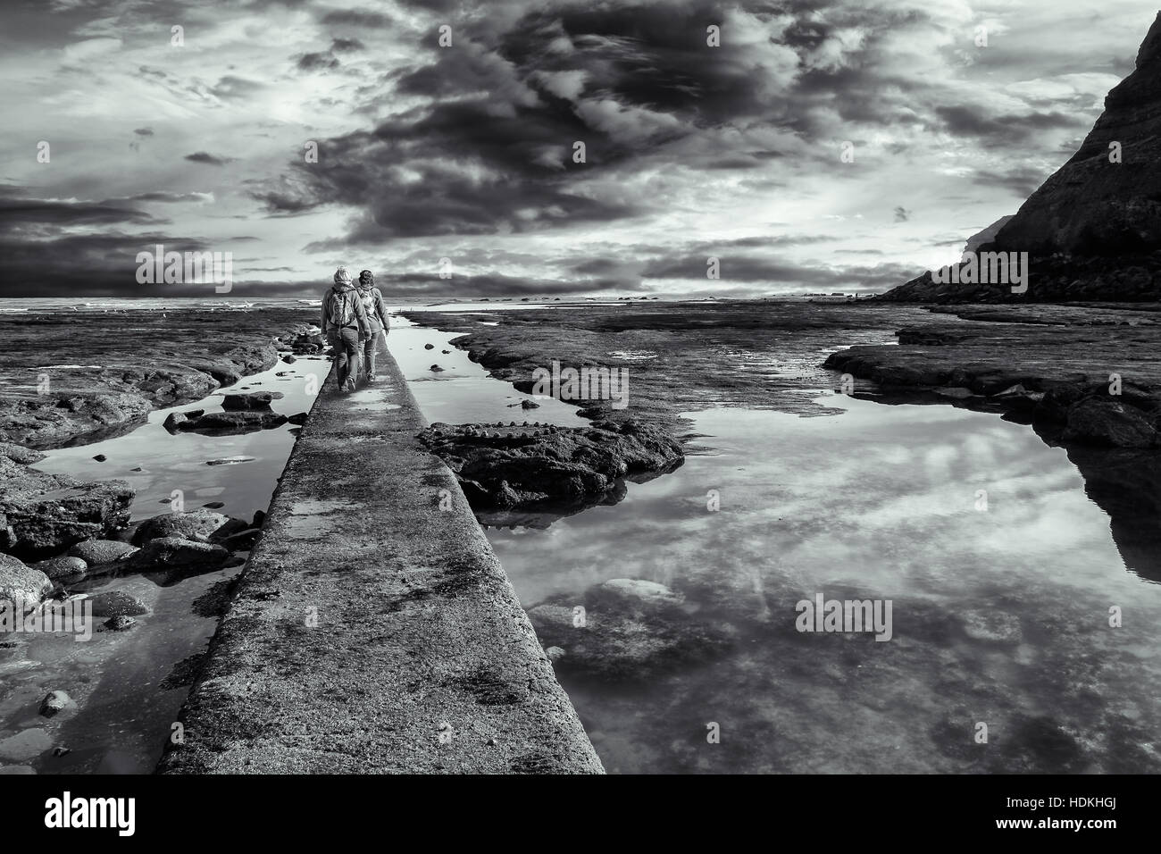 Walkers on the long path at low tide with reflections in the rock pools ...