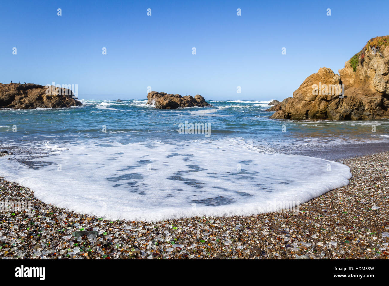 Beautiful sea glass in a variety of colors with blue waves and sky in ...