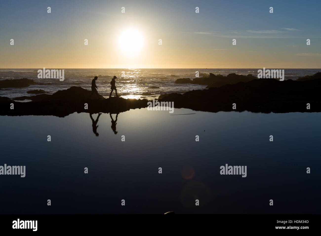 couples silhouette walking on a rocky trail reflecting on a tidal pool ...