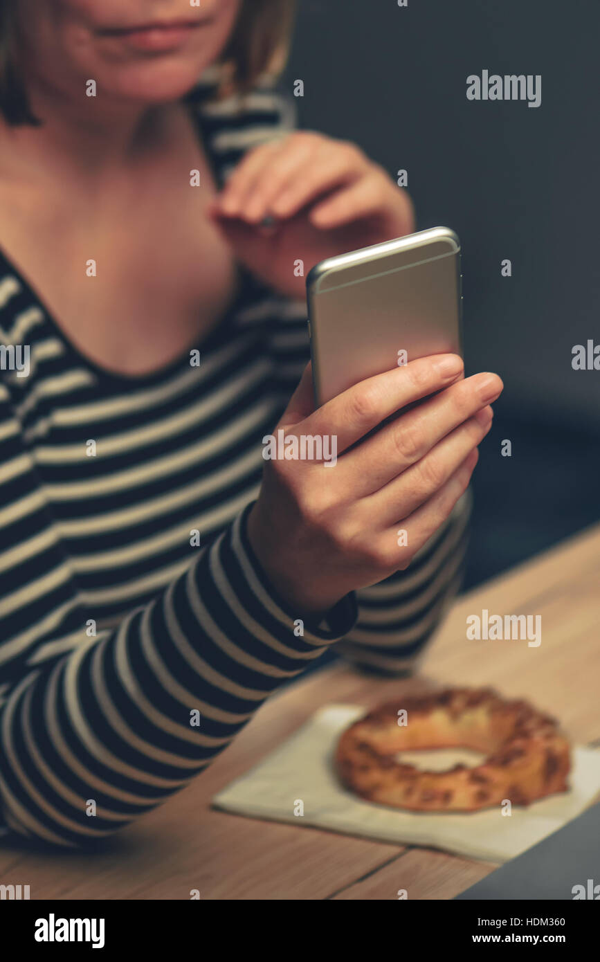 Woman eating sesame bagel and using mobile phone in office while ...