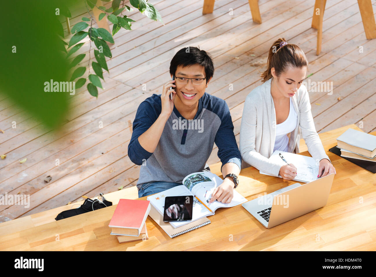 Two happy young students studying and talking on cell phone in outdoor ...