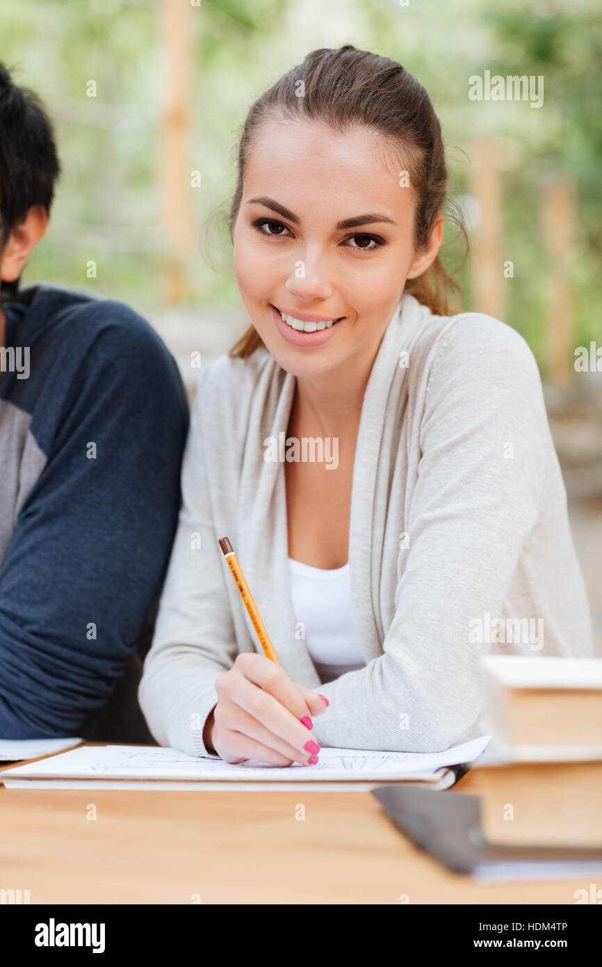 Smiling attractive young woman sitting and writing at the table Stock ...