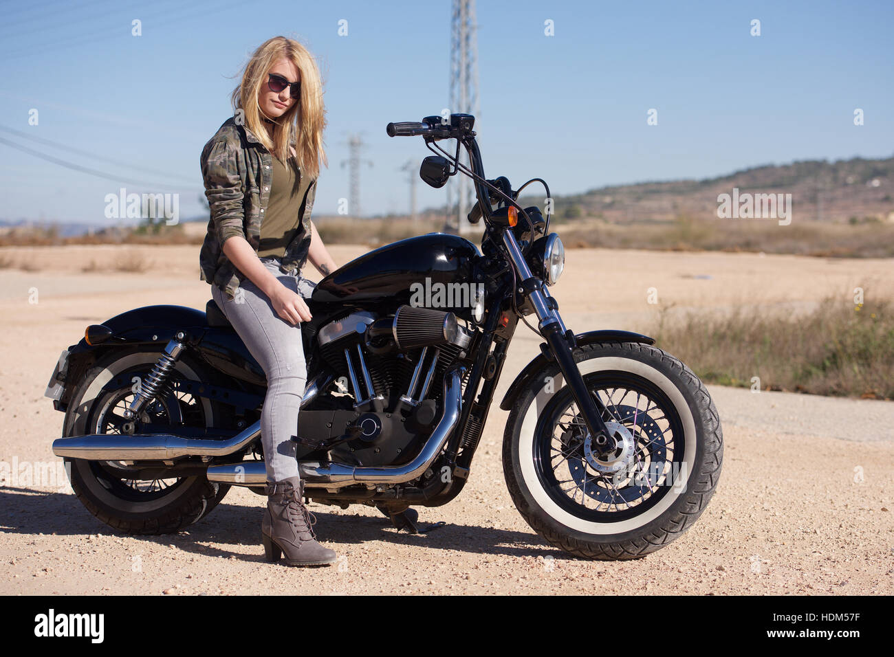 Blonde teenage girl on black motorcycle in desert looking environment ...