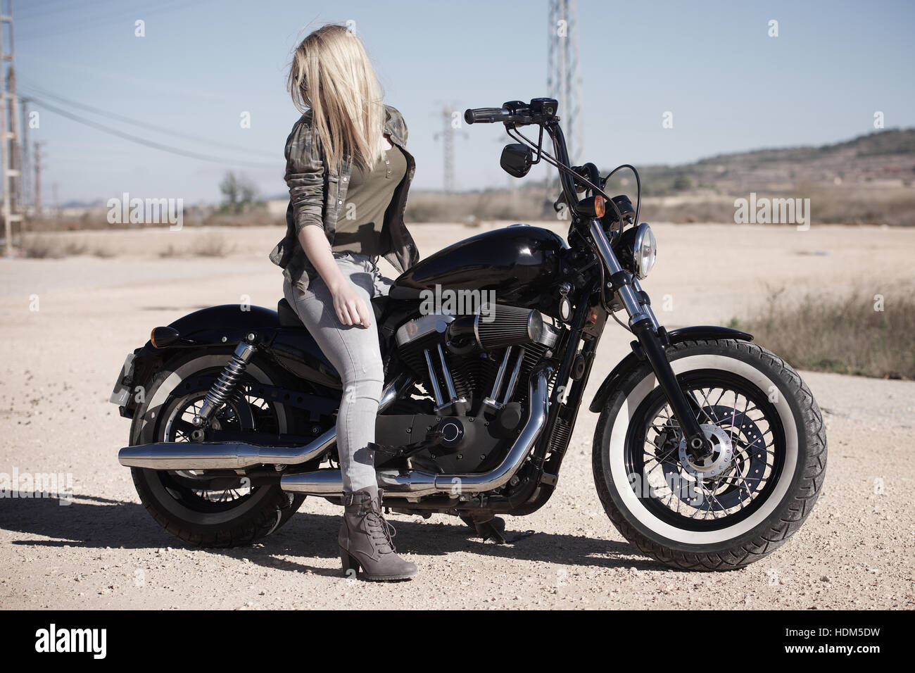 Blonde teenage girl on black motorcycle in desert looking environment ...