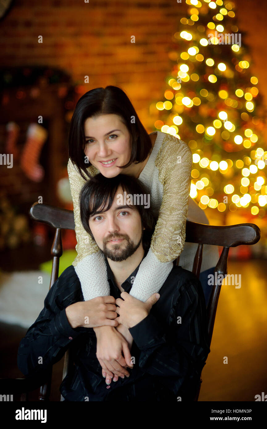 Young woman embraces man sitting in a chair. The dark wall of the room ...