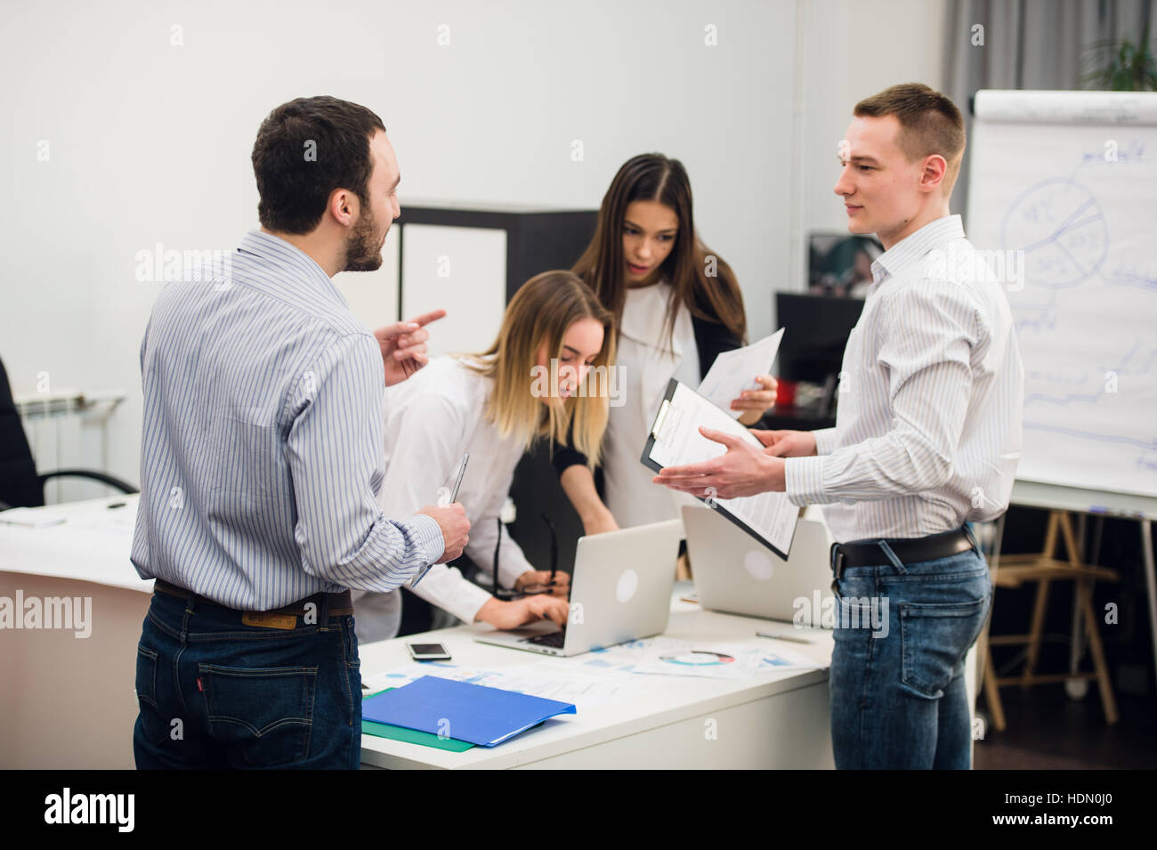 Four young business people working as a team gathered around laptop ...