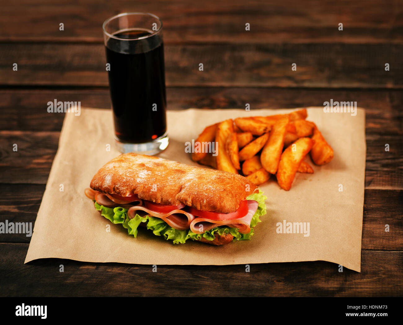 Cheeseburger with potato wedges fried and glass of cola on paper served ...