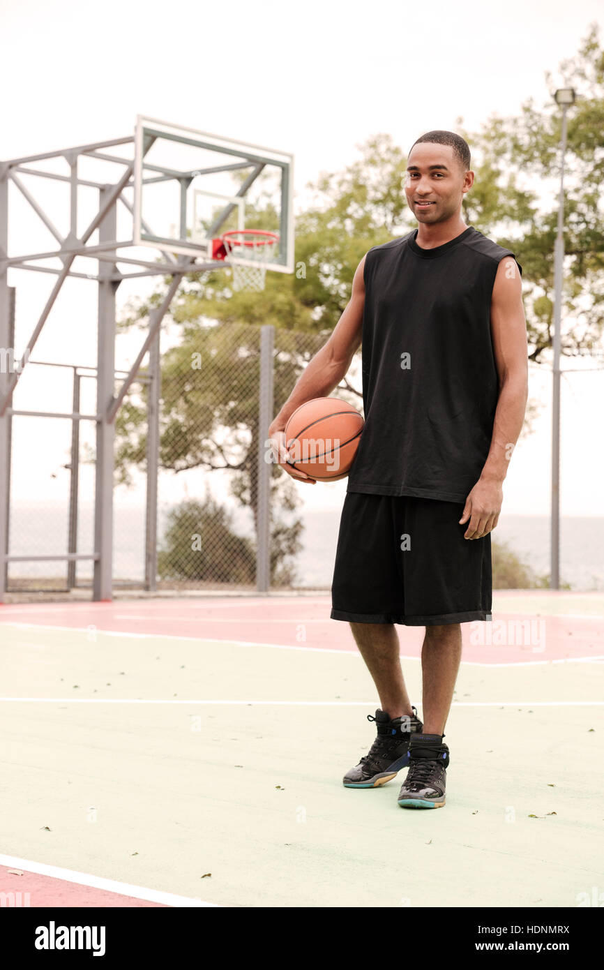Photo of african smiling basketball player standing in the street with ...