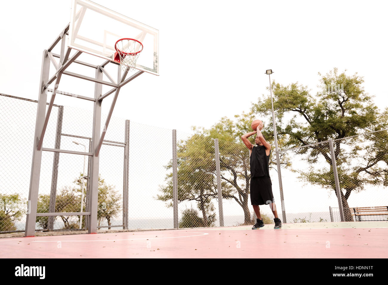 Photo of young basketball player practicing in the street with trees on ...