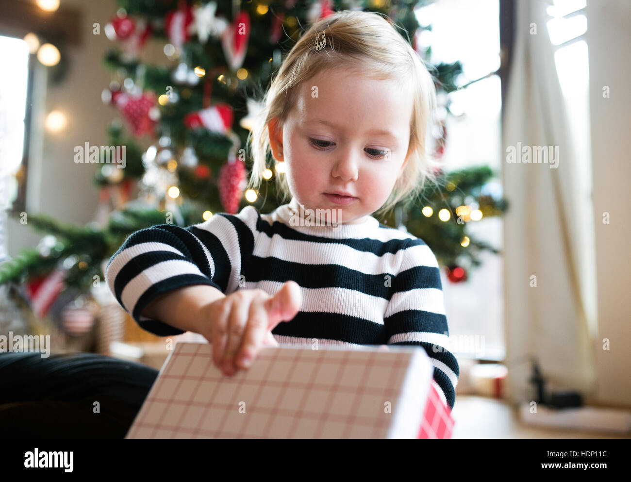 Little girl at the Christmas tree opening present Stock Photo - Alamy