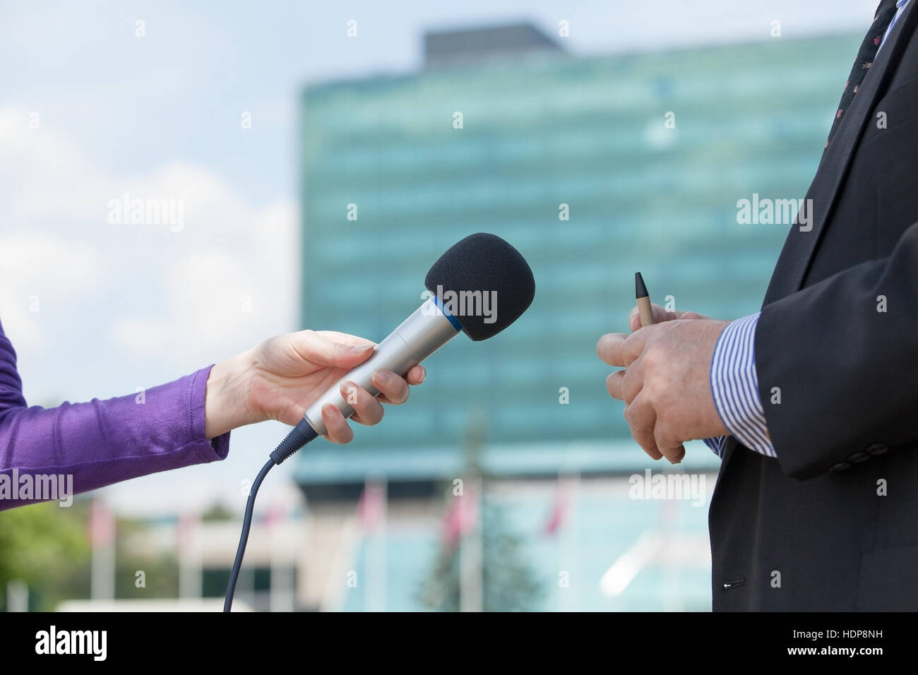 Female reporter interviewing business person, corporate building in ...