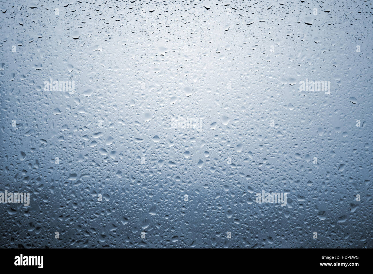 Drops of rain on a window glass with very diffuse landscape pale blue ...