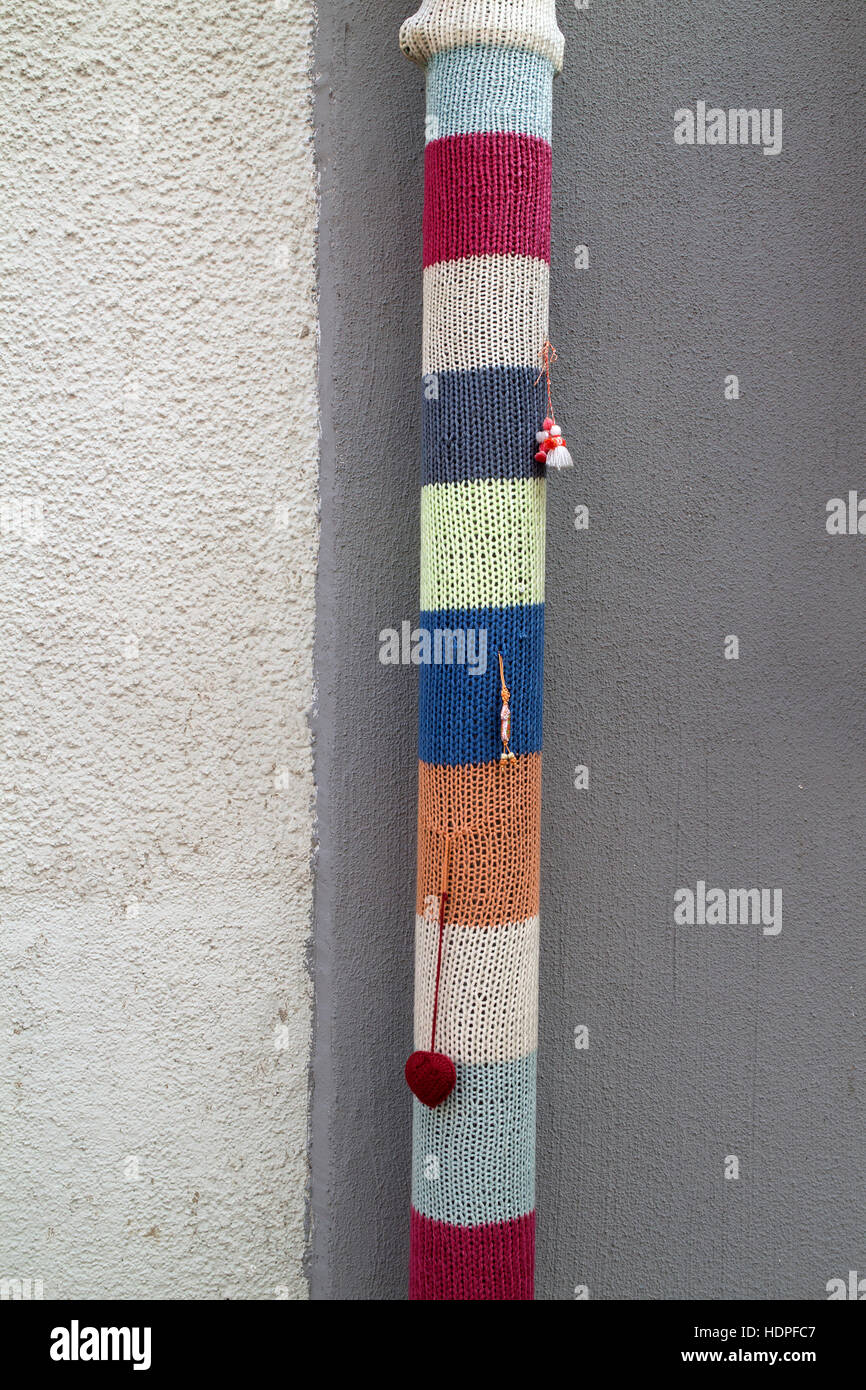 A drain pipe wrapped in a striped knitted cover with bobbles ...