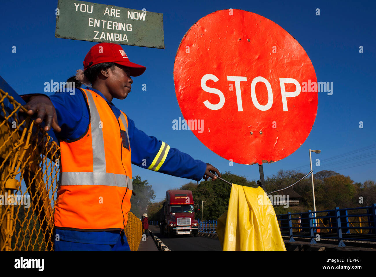 A woman controls the traffic between Zambia and Zimbabwe. A STOP sign ...