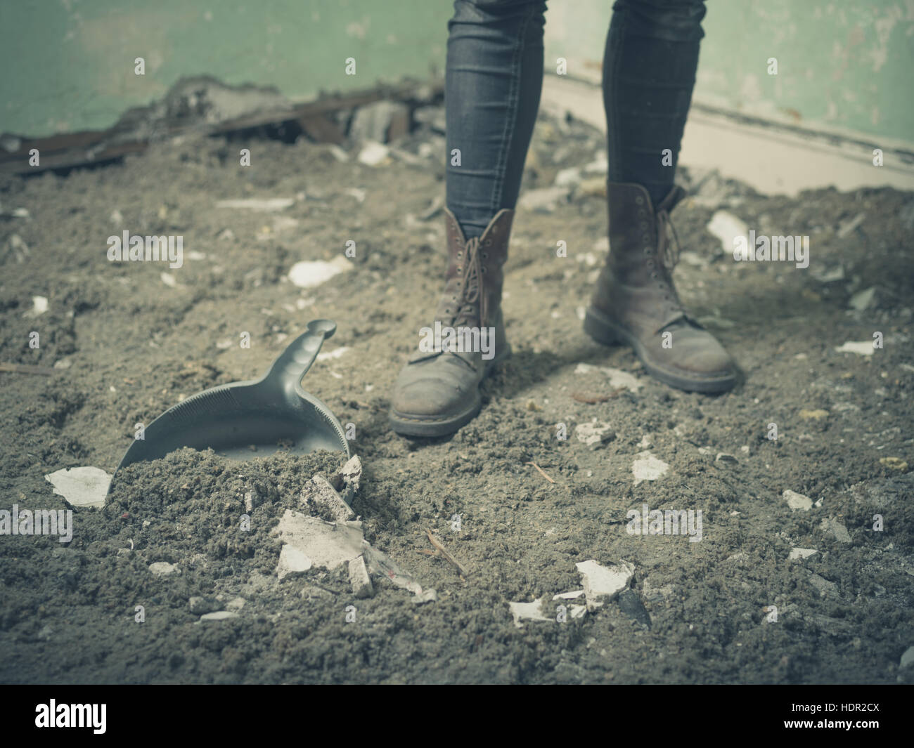 The feet of a person wearing boots by a dustpan on a floor covered with ...
