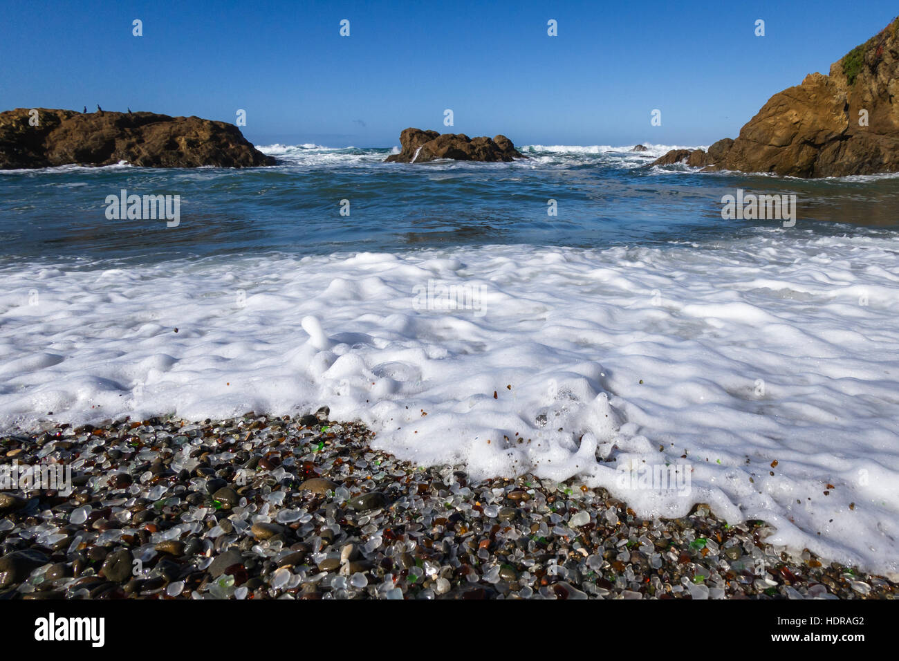 Beautiful sea glass in a variety of colors with blue waves and sky in ...