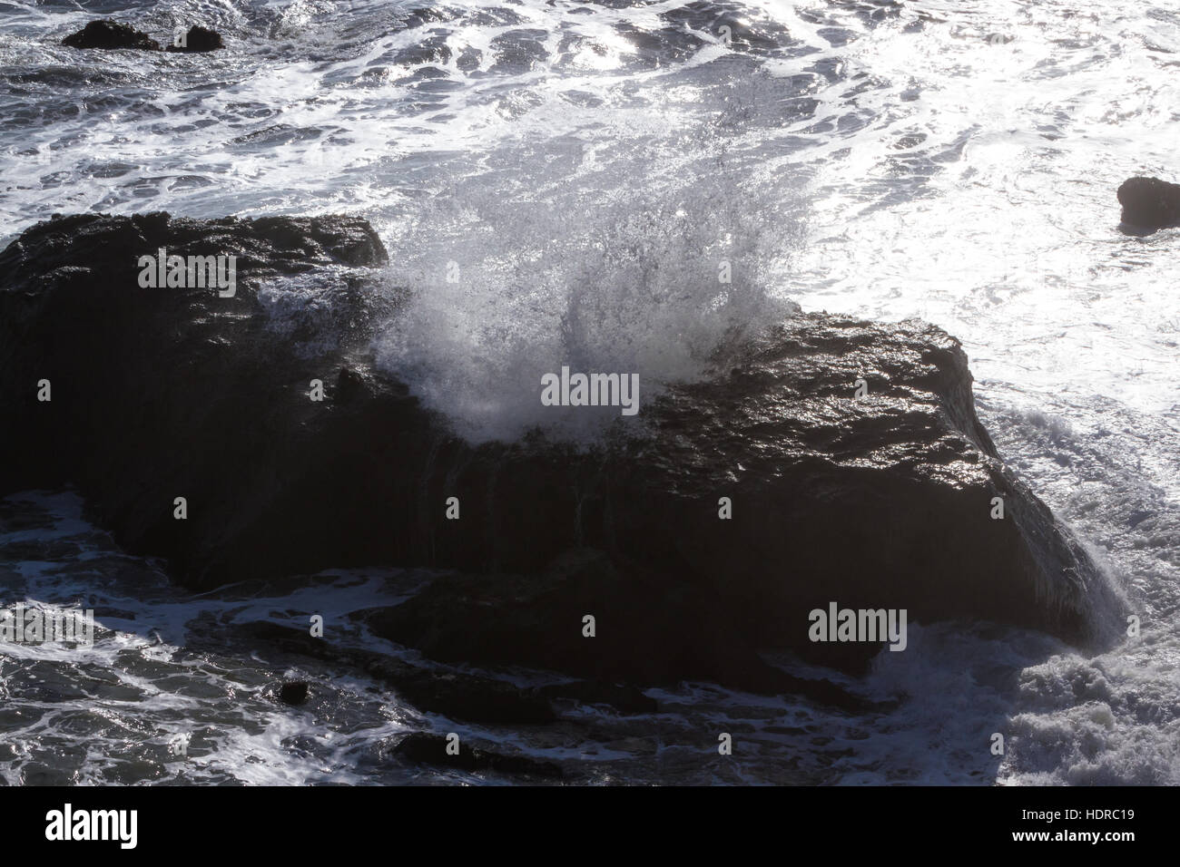 high contrast image with a dark large rock and powerful waves crashing ...