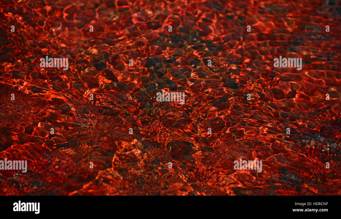 Abstract red color running water stream deflection flowing over stones ...