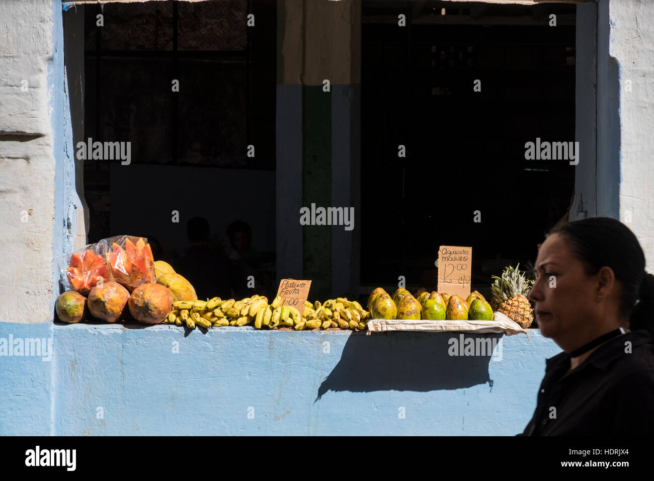 Woman passing display of fruit and veg for sale on a sunlight ...