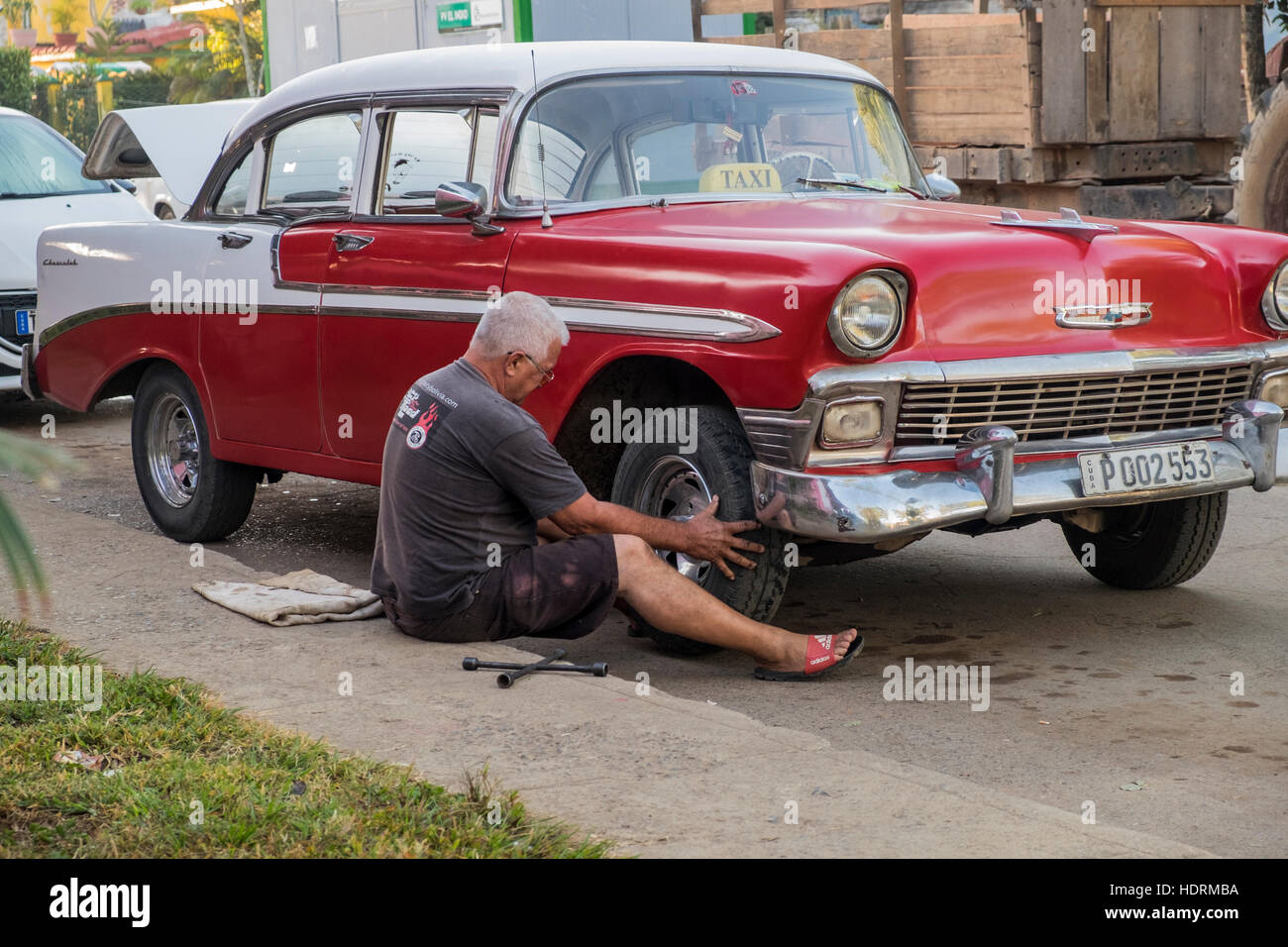 Taxi driver repairing wheel on his car, 1950s old American Chevrolet ...