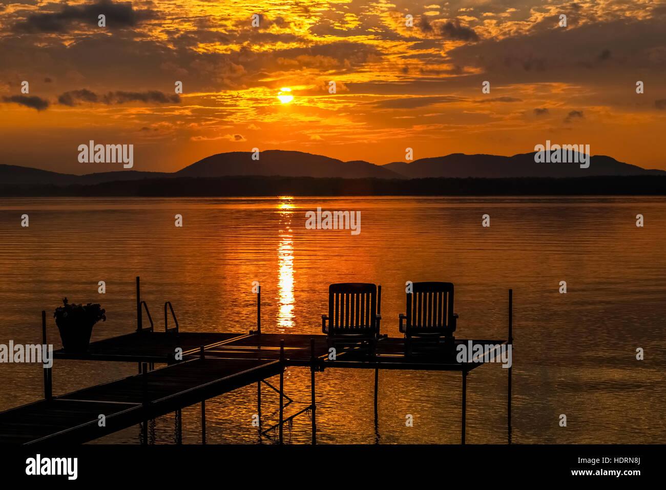 Sunset on lake with silhouetted chairs on wharf; Knowlton, Quebec ...