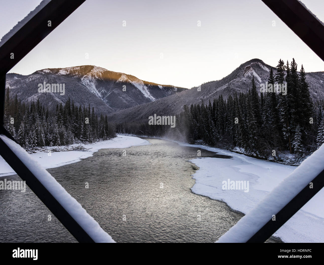 A landscape with snow along the shoreline of a lake and a mountain ...