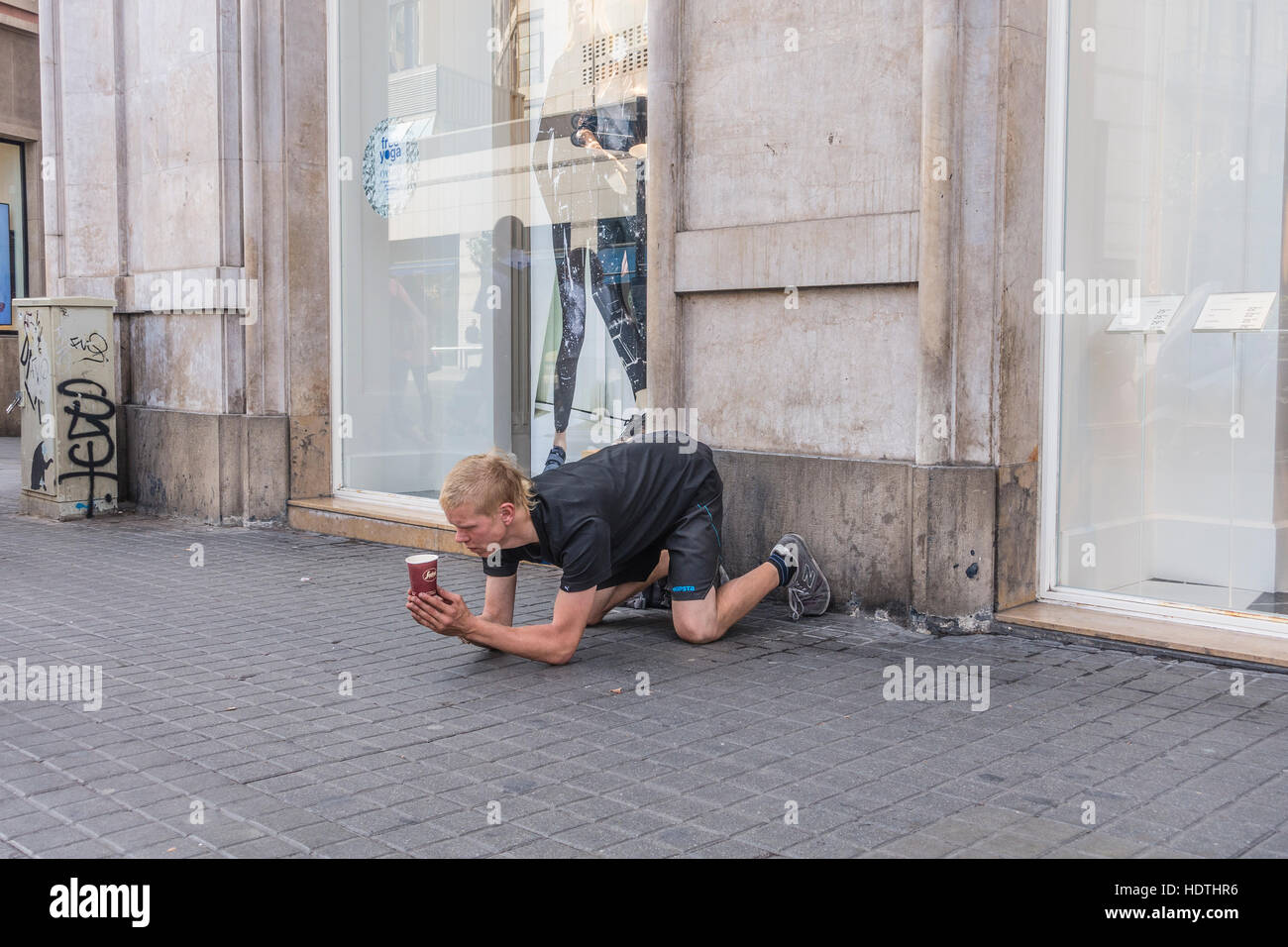 A 20s male beggar knelling on a sidewalk in the busy part of Barcelona ...