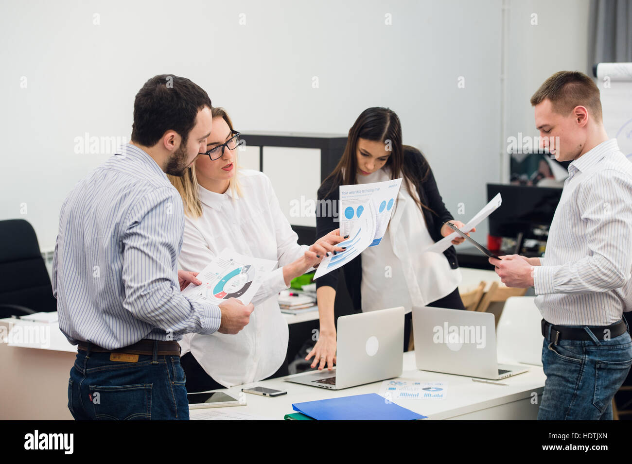 Four young business people working as a team gathered around laptop ...