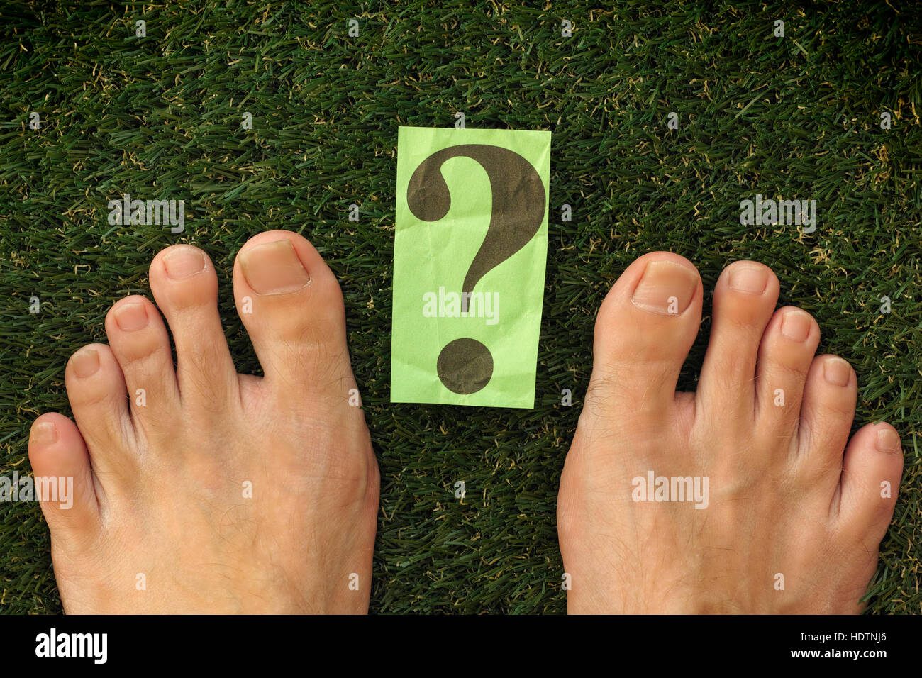 Feet on green grass which has a question mark on it. Close up Stock ...