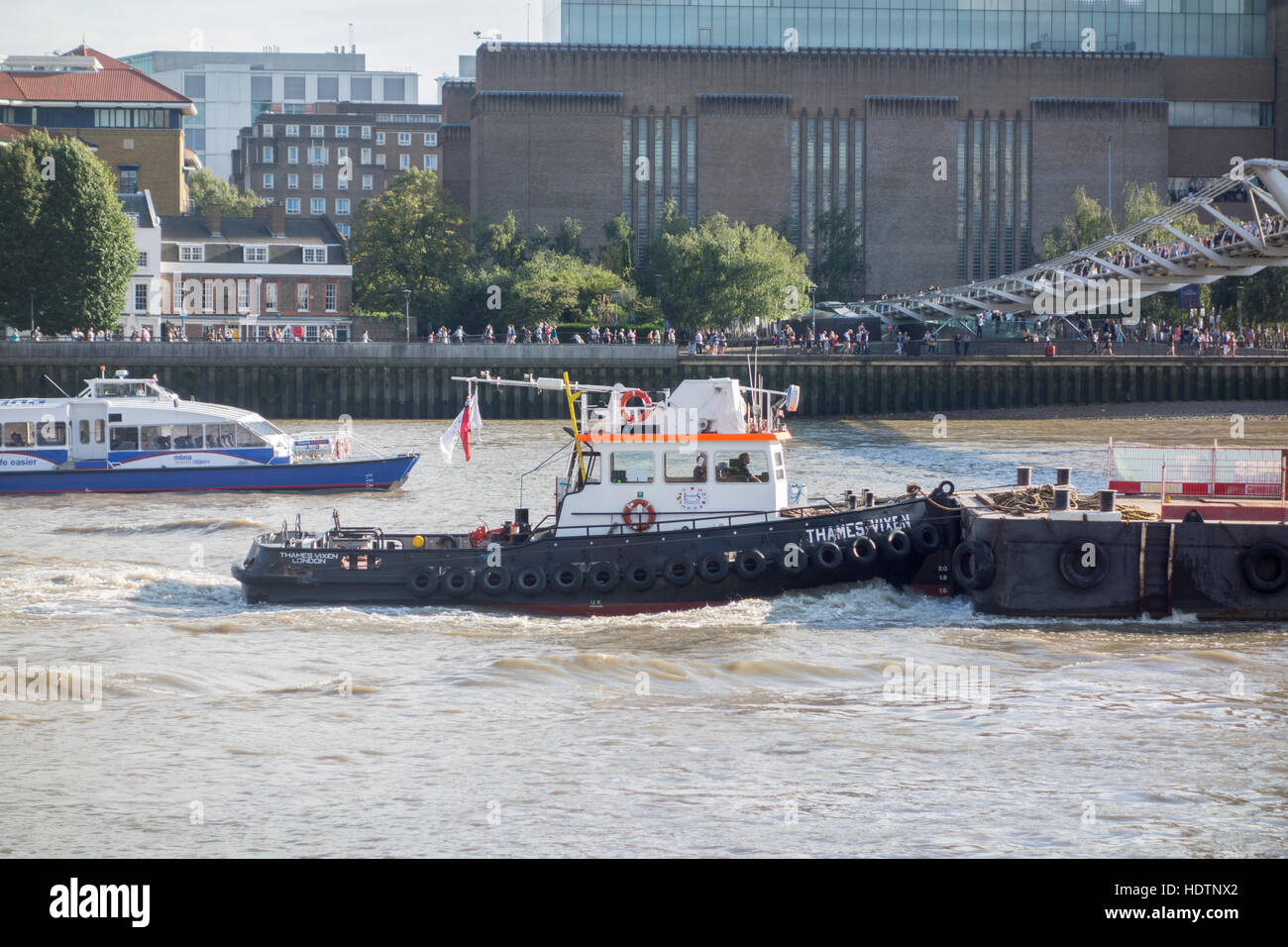 Tug boat pushing a barge under Millennium Bridge on the River Thames ...