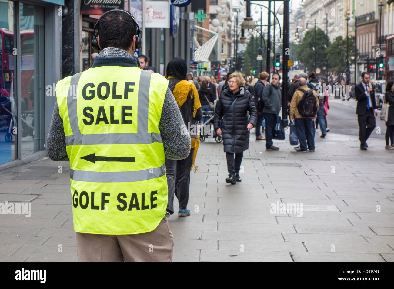 Shoppers passing man wearing high visibility jacket with Golf Sale ...